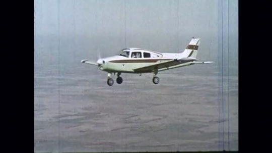 UNITED STATES: 1970s: Small plane flies in sky above ground. Plane ...