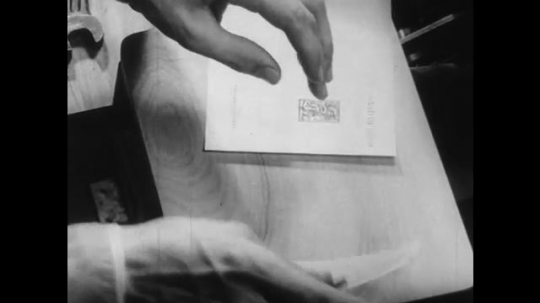 1950s: UNITED STATES: man applies paste to paper. Man cuts away excess ...