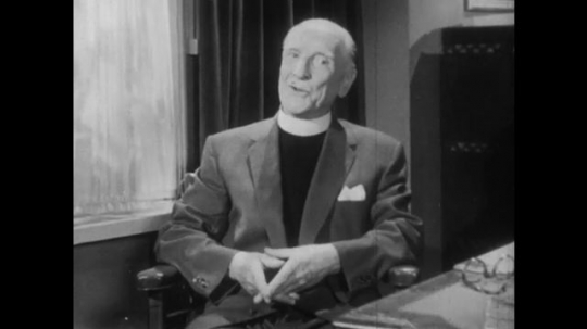 1950s: Priest sits behind desk, hands folded together, and talks ...