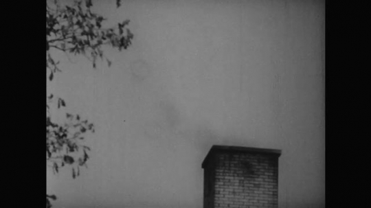 1950s: Dark smoke drifts out of chimney. Man in cap draws diagram for ...