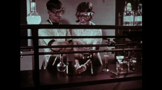 1970s: Students work at laboratory table. Boy and girl look at each ...
