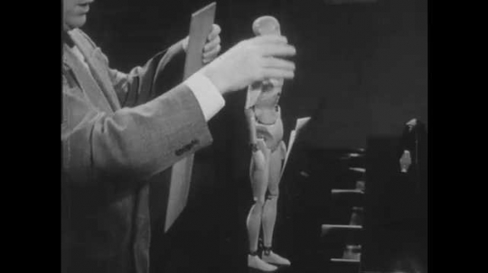 1950s: Man points to several spots on model of human body. Man holds ...