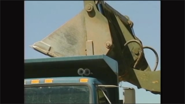 2000s: Man operates front end loader, lifts bucket over dump truck ...