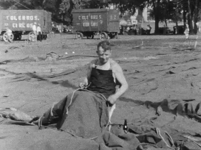 1940s: Circus worker mending tent takes drink from bottle. – Archival ...