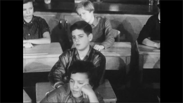 1950s: Teacher stands and speaks. Students sit in classroom. Boys speak ...
