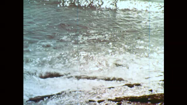 1960s: Waves crash on shoreline. Hand places beaker of sea water on ...