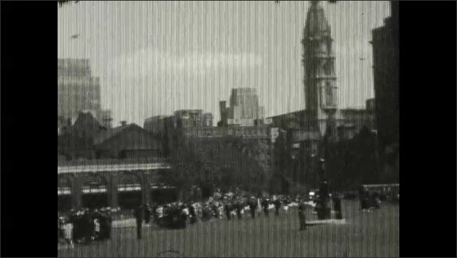 1930s: a busy street as people wait on the sidewalk for a parade to ...