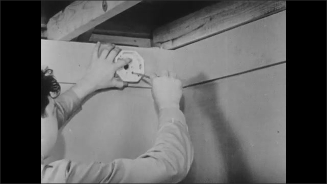 1940s: UNITED STATES: man places junction box above entrance in hallway ...