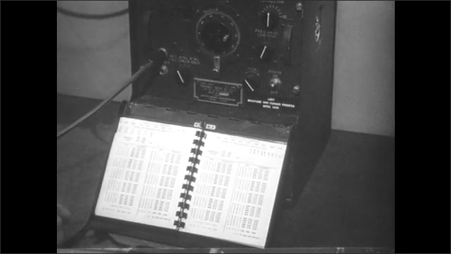 1950s: Man moves machine in lab. Hand turns page of booklet. Close up ...