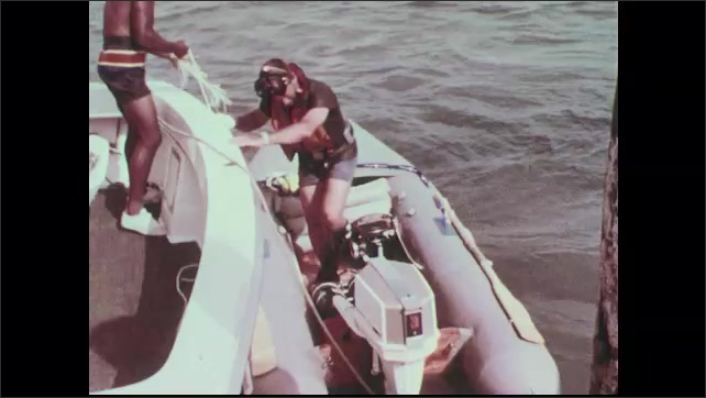 1960s: Scuba diver loads equipment into dinghy. Deckhand comes aboard ...