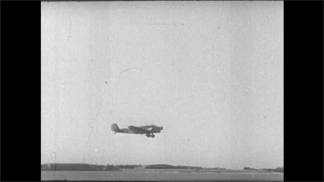 1930s: Long shot, paratrooper dropping to ground. Plane starting. Plane ...