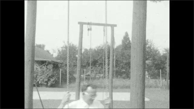 1920s: Women and man sit on swing. Man swings on swing. – Archival Footage