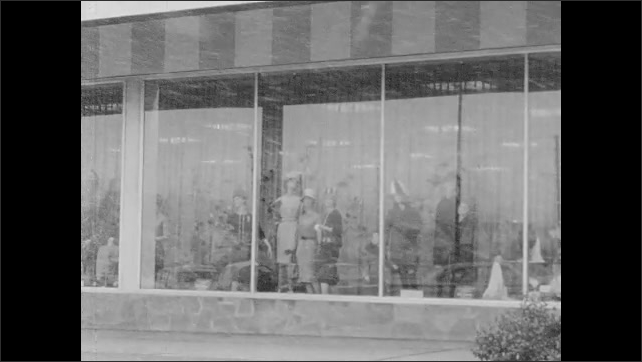 1960s: Cars drive through shopping center parking lot. Storefront ...