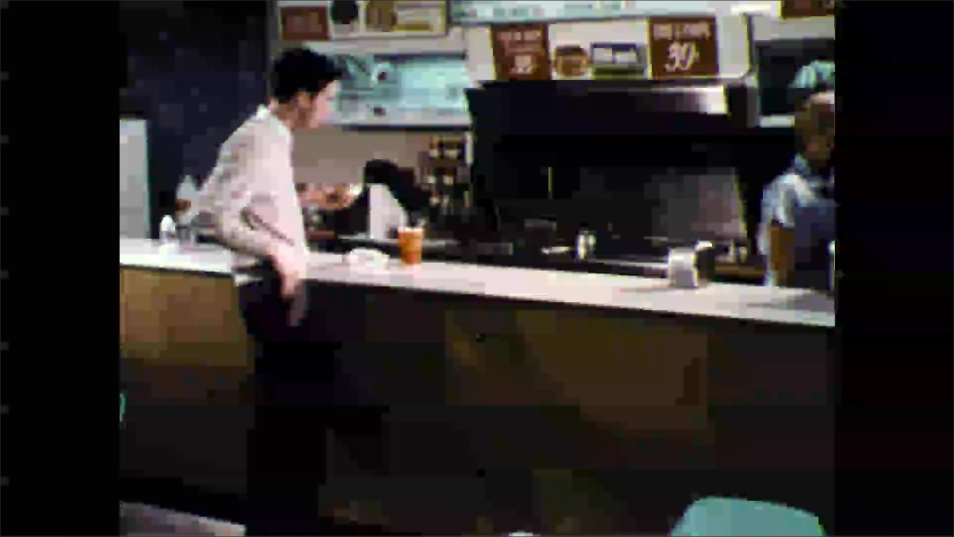 1960s: Young man stands at fast food restaurant counter, unwraps, eats ...