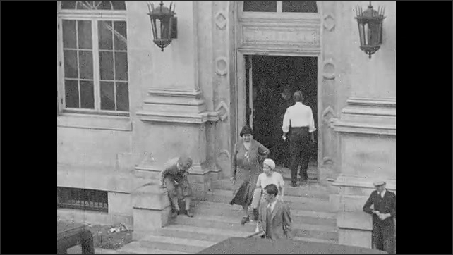 1930s: UNITED STATES: people leave building. Boy sits near steps of ...