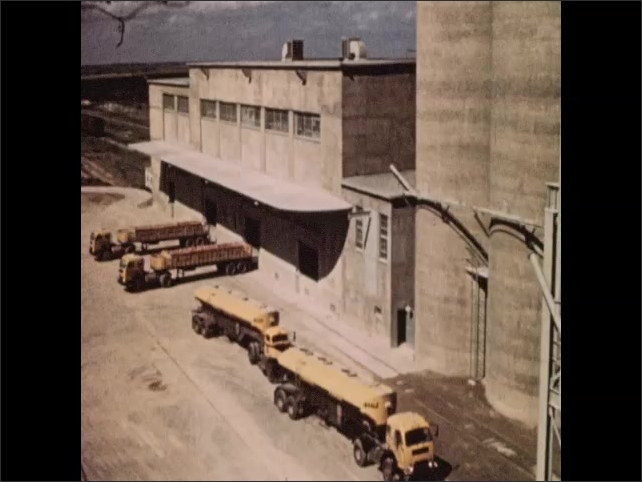 1950s: Industrial cement storage silo. Transport trucks parked around ...