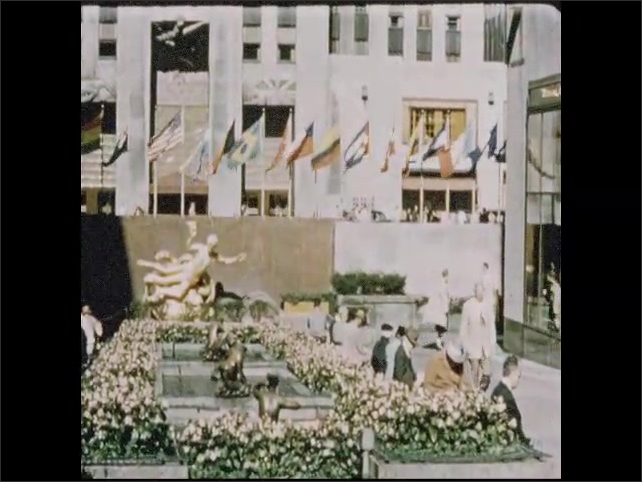 1950s: Two women look up, smile, stand in front of statue of Atlas ...