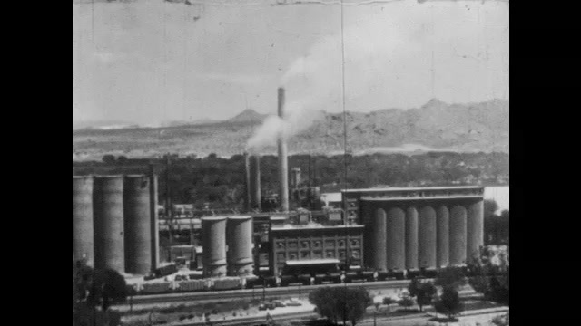 1950s: Factory with large silos, smoke stacks billow. Heavy truck ...