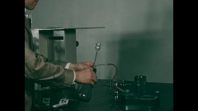 1950s: Man in laboratory places tube inside of beaker. Man pours clear ...