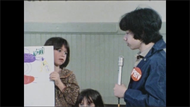 1970s: School cafeteria. Boy reporter interviews students holding ...