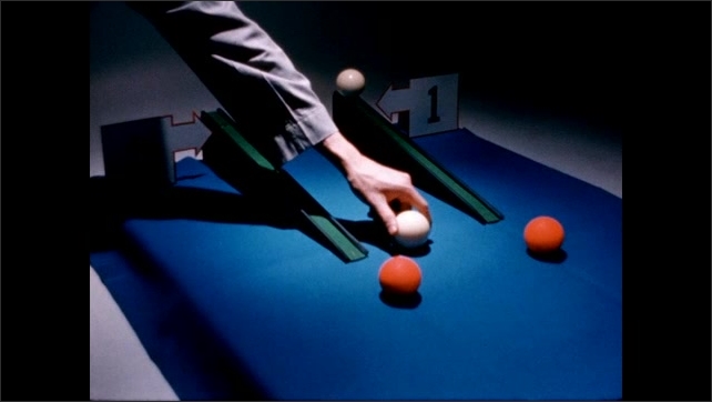 1960s: Plane flies through sky. Hand releases ball on ramp. White ball ...