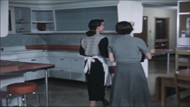 1950s: Two teen girls walk out of home ec classroom kitchen and look at ...