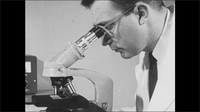 1950s: Man places slide on microscope, looks through microscope ...