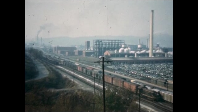 1950s: Train drives past large refinery and parking lot. – Archival Footage