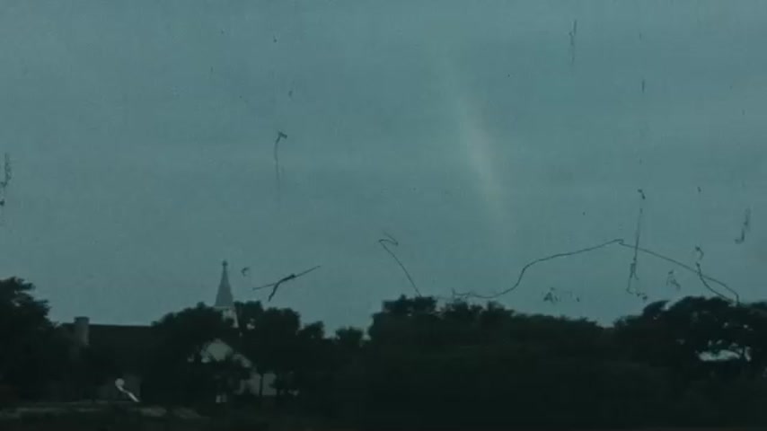 1960s: Faint rainbow in sky over building. Sun shines behind clouds ...