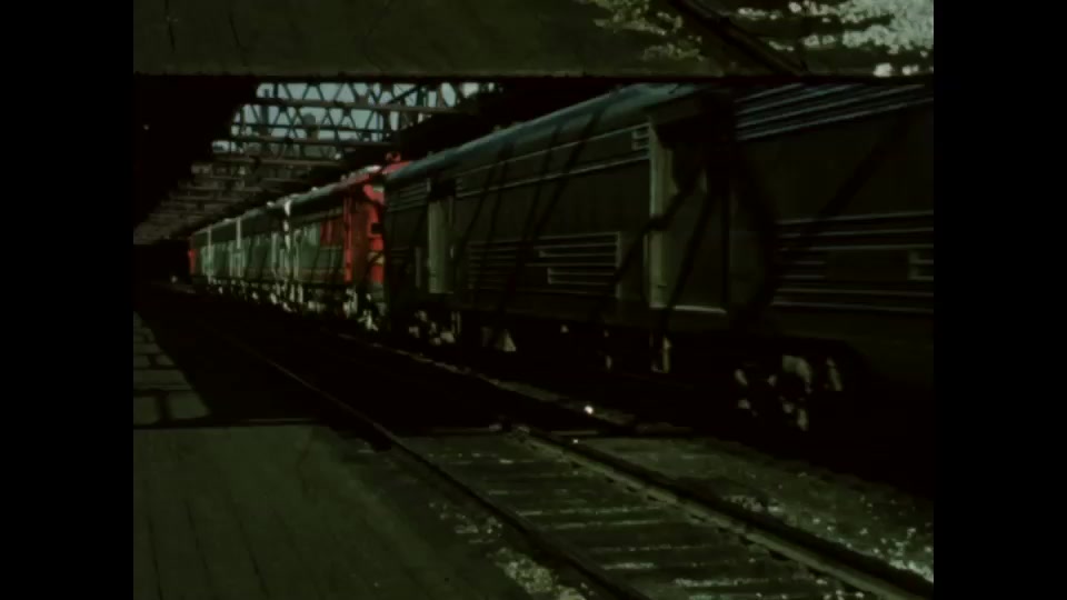 1960s: Train moves on tracks under metal structure. – Archival Footage
