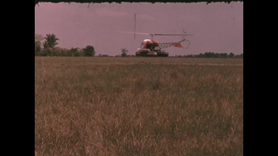 1960s: Helicopter flying over field, tilt down to wire unrolling from ...
