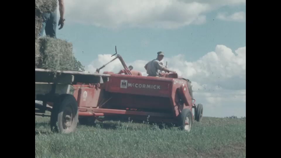 1960s: Two men ride on tractor and hay baler, collecting grass and ...