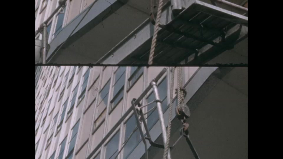 1960s: City street. Men on sidewalk pull ropes to raise window ...