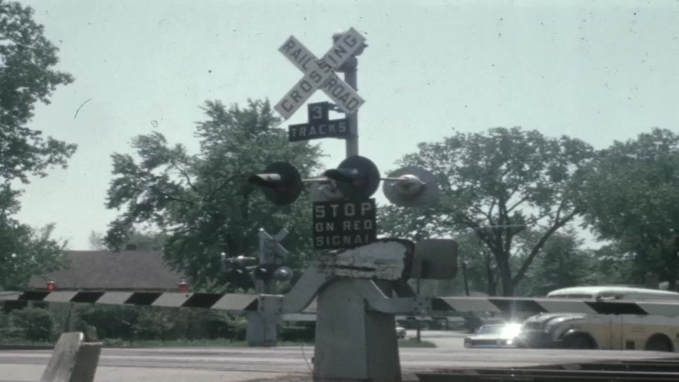 1960s: Railroad crossing sign with barrier gate. Train passes ...