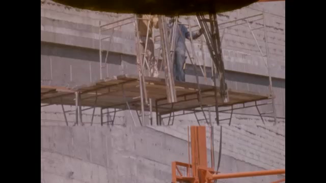 1970s: men lifting scaffolding off crane, man hand-mixing cement ...