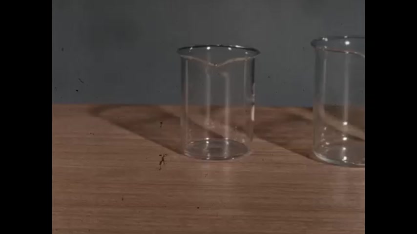 1960s: Hand places card with numbers in front of empty glass beaker ...