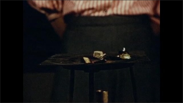 1950s: Fire burning in pit. Hands move objects on grate over flame ...