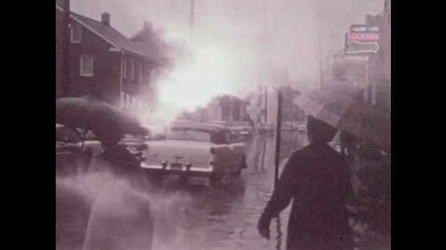 1960s: cars driving and pedestrians walking in rainy city, clouds over ...