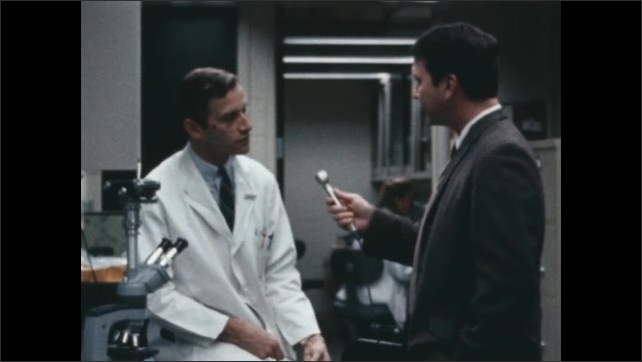 1960s: Lab, man wears white lab coat, sits next to microscope. Man ...