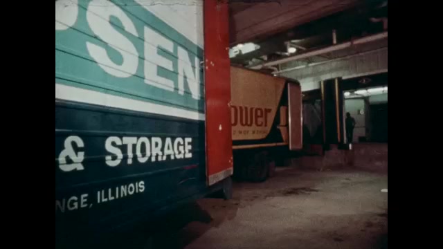 1970s: Moving trucks back up toward loading docks. Workers roll in ...