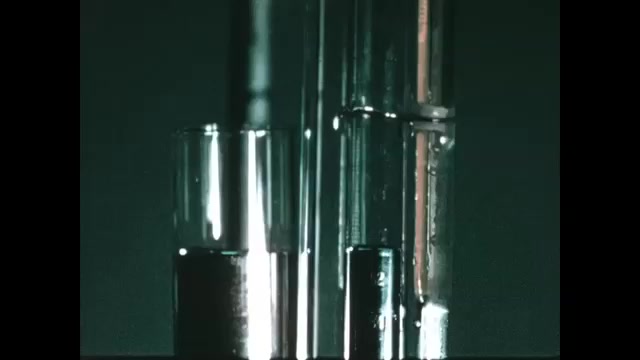 1950s: Tubes and flask and tubing on apparatus. Man in suit explains ...