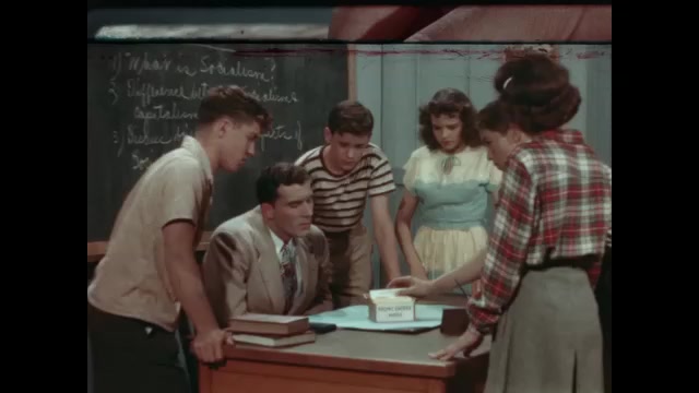 1940s: Kids in classroom around desk, boy walks to box. Hand looks ...