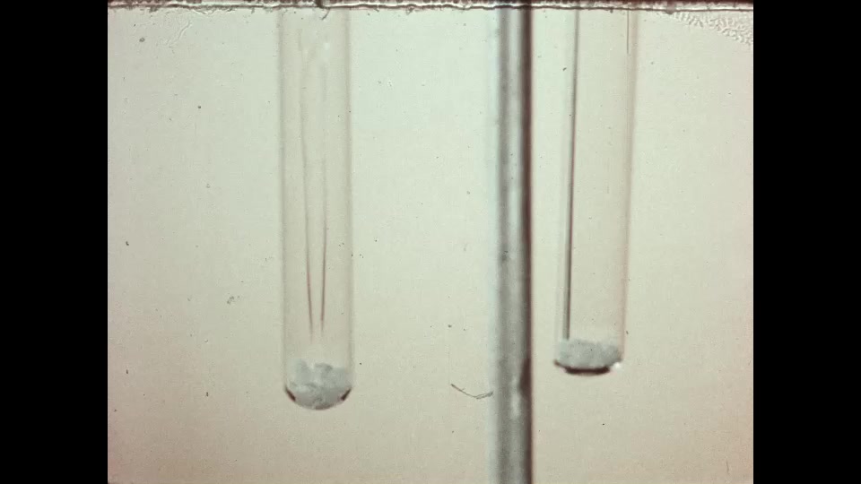 1960s: Two test tubes with crystals in them. Left test tube bubbles and ...