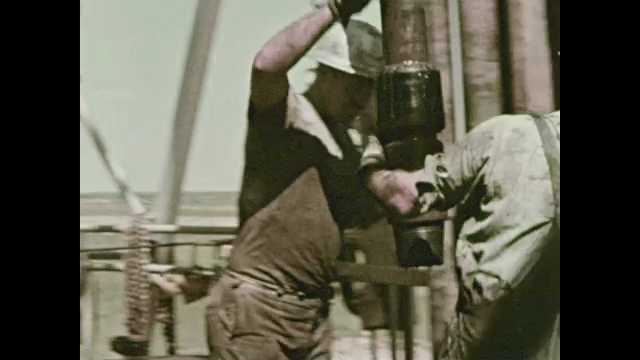 1960s: Men move large metal part together. Man climbs down tower. Men ...