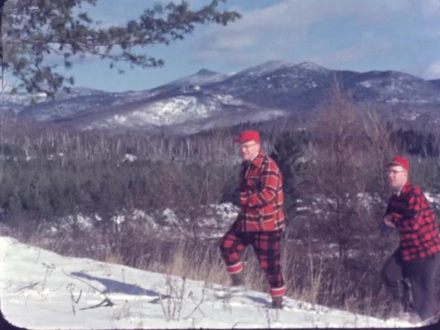 1950s: Two men in hunting clothes, carrying rifles, walk up snowy hill ...