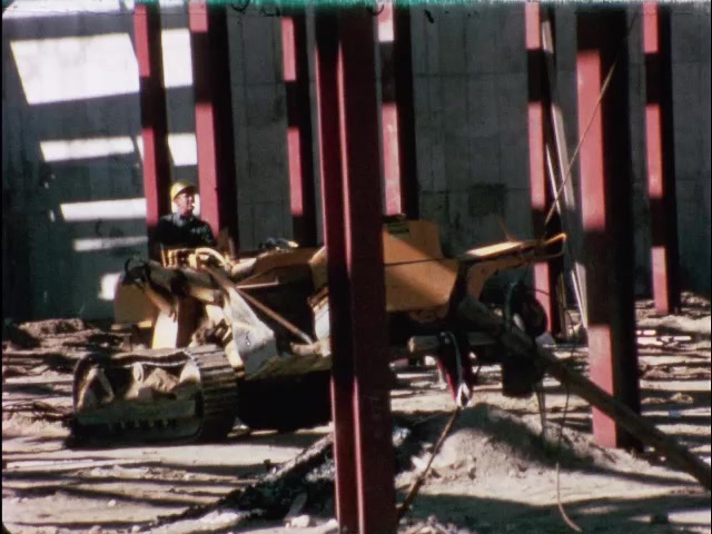1960s: Man drives machine at a construction site, structure of steel ...