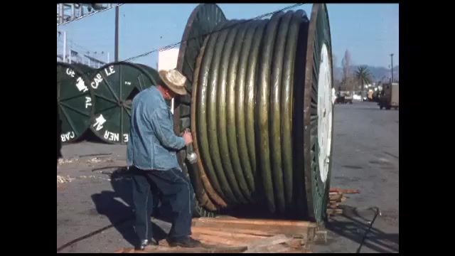 1950s: man poses with large spool of cables, electrician inspects ...
