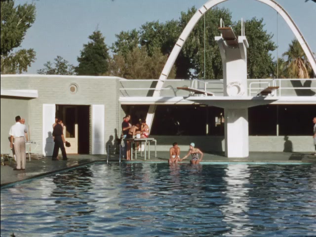 1950s: UNITED STATES: guests relax by hotel pool. Lady chats to man by ...