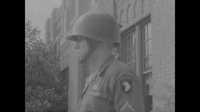 1950s: Soldier stands in front of high school. Soldiers march up steps ...