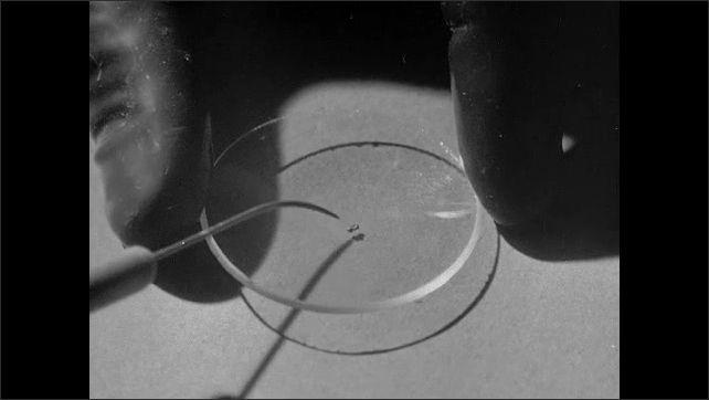 1940s: Man carries rod with metal pipe hanging from rope. Man looks ...